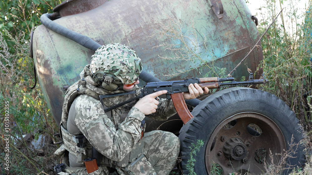 A soldier in full combat gear aims his assault rifle while taking cover ...