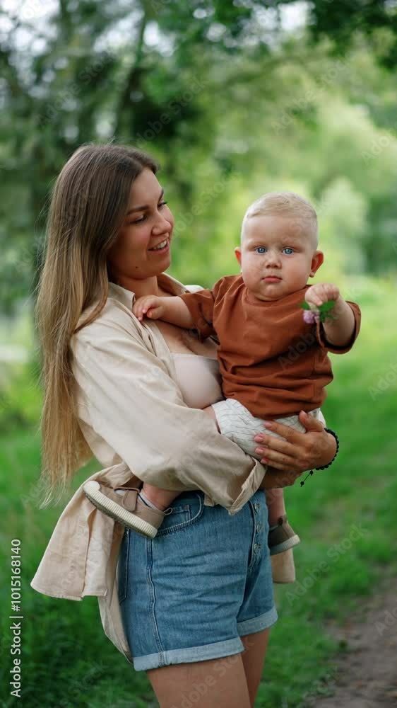 Blond Caucasian woman with long hair holds a toddler boy in hands ...