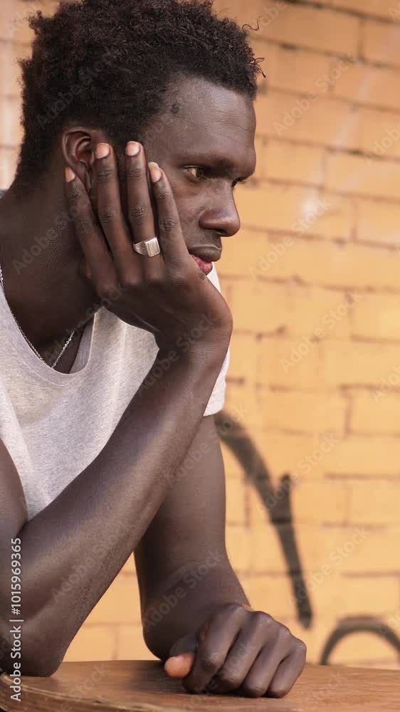 Vertical. Side view of a young North African man sitting alone at a ...