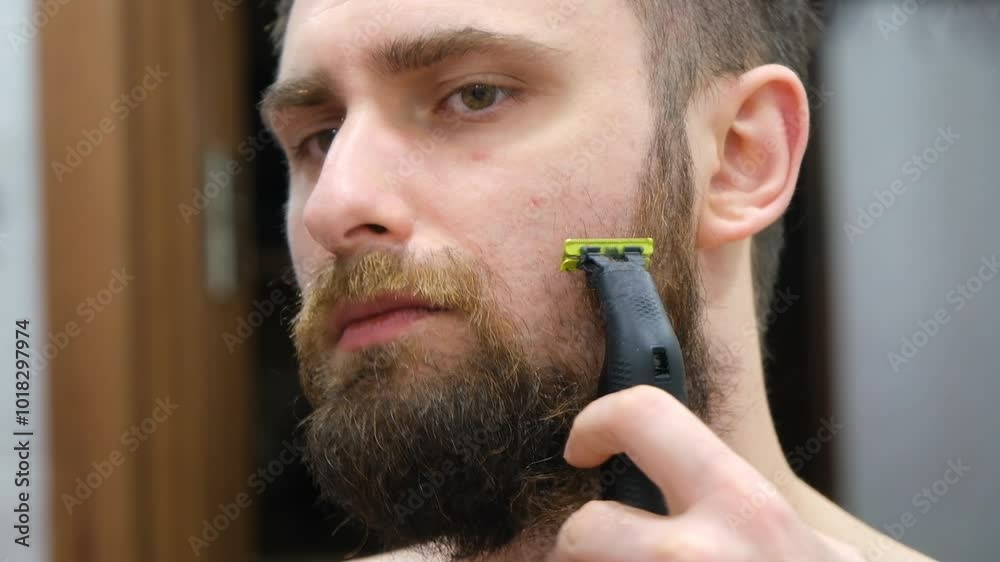The man shaves his big beard. The guy shaves off his big beard. Young ...