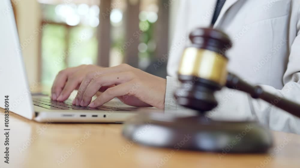 A woman is typing on a laptop while a judge sits behind her. The laptop ...