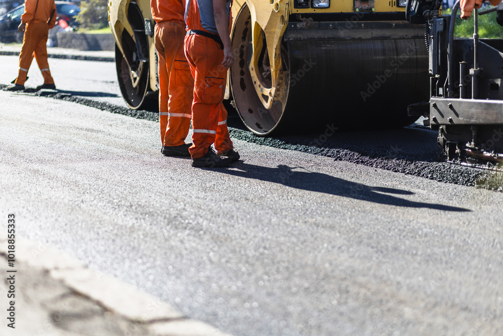 Road construction workers operating heavy machinery on a sunny day ...