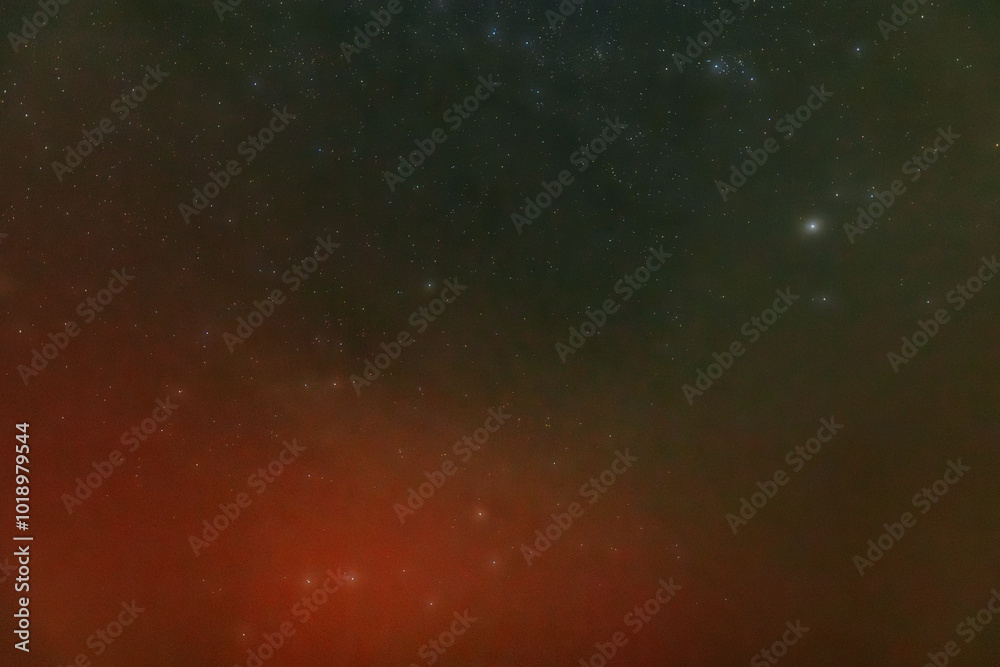 A peaceful night sky filled with faint stars and a soft red aurora glow ...