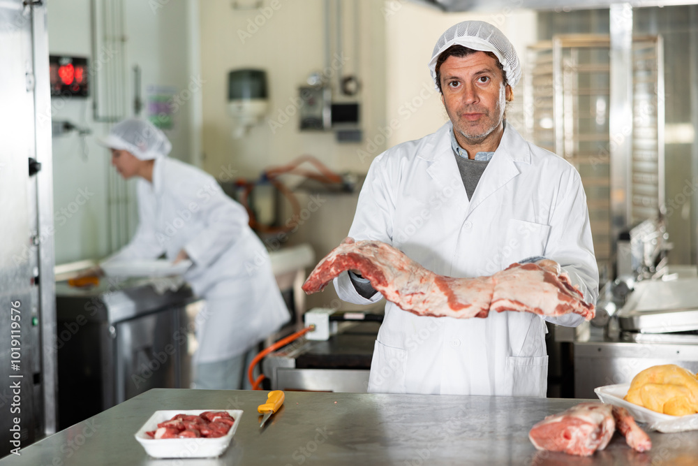 Professional butcher in white uniform standing at meat cutting table ...