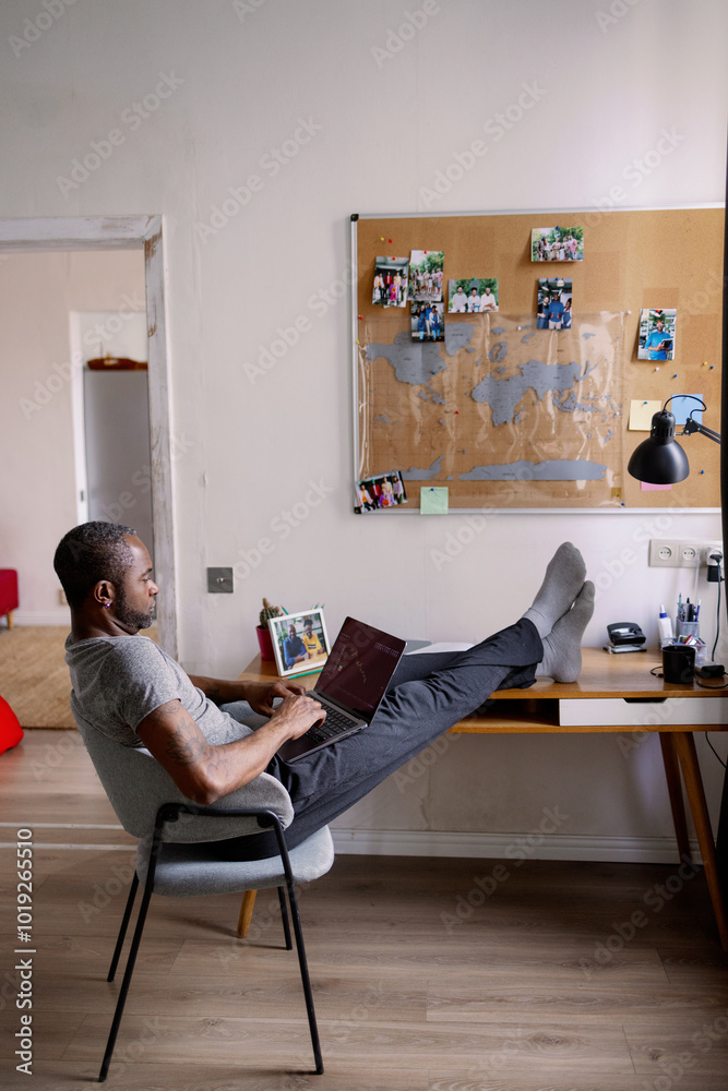 Side view of black man watching and typing laptop on chair at desk ...