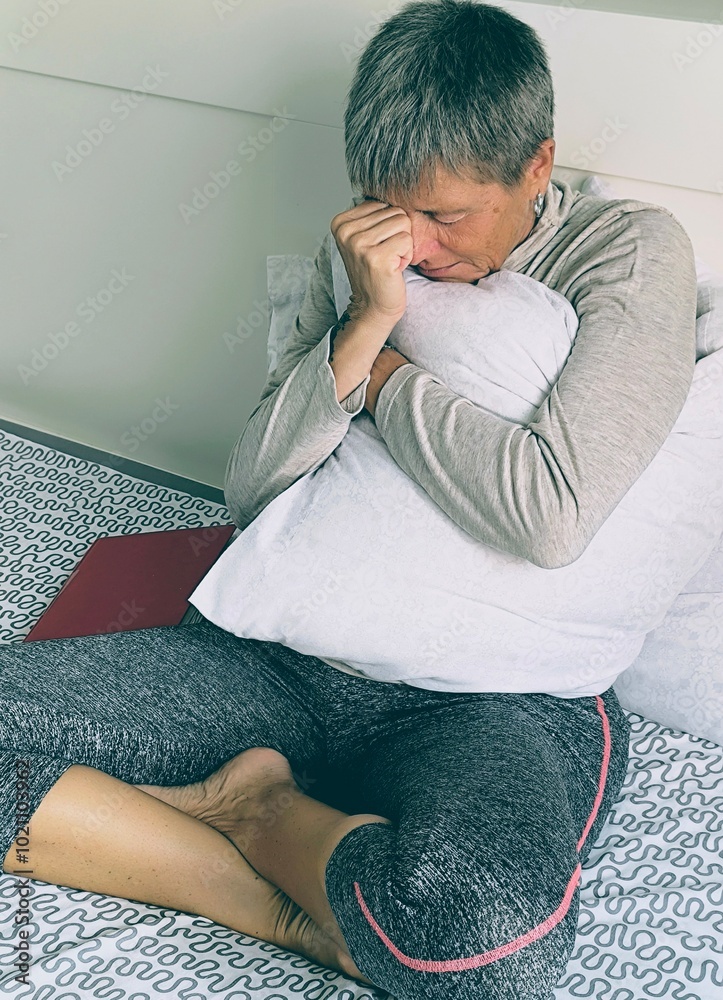 Young woman sitting on bed with legs crossed and hands covering her ...