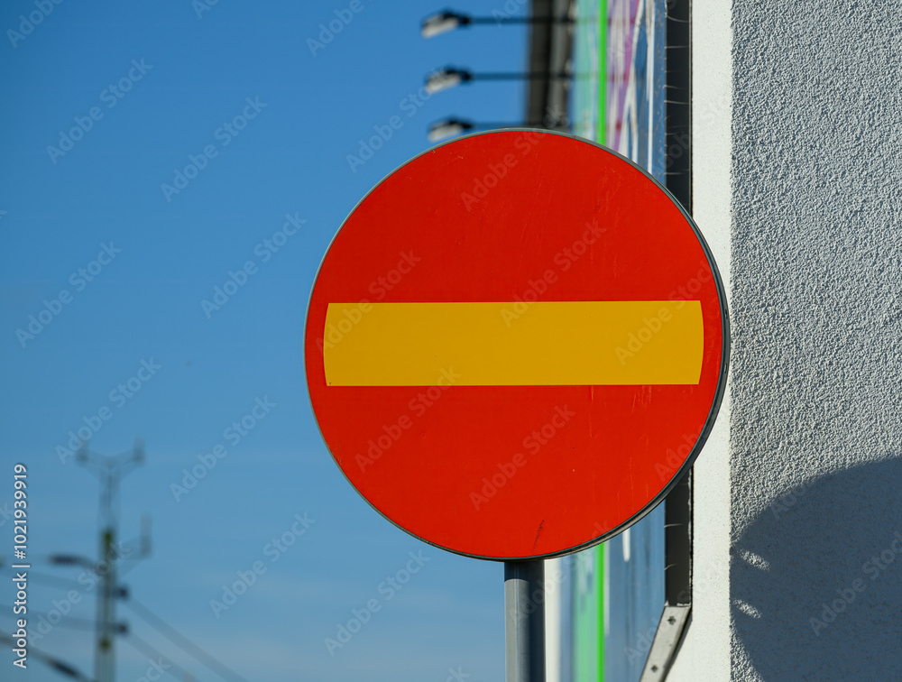 A bright red no entry sign with a horizontal yellow bar is mounted on a ...