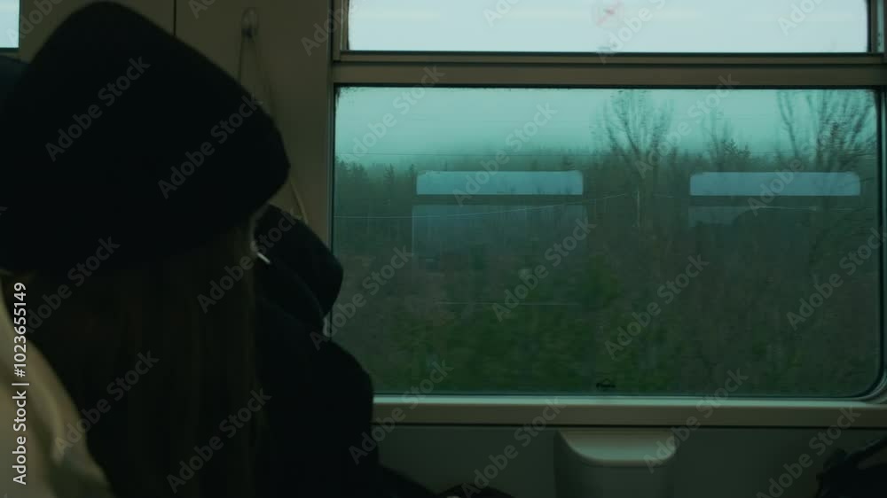 A girl looks out the window on a train. Passengers are resting in a ...