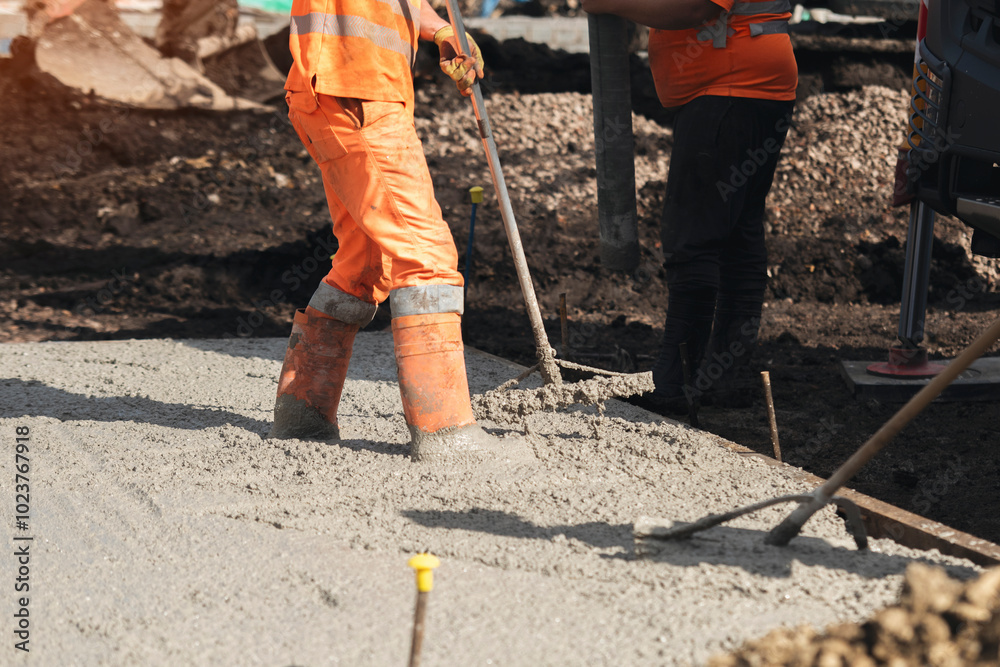 Construction workers pouring concrete on sunny day at building site in ...