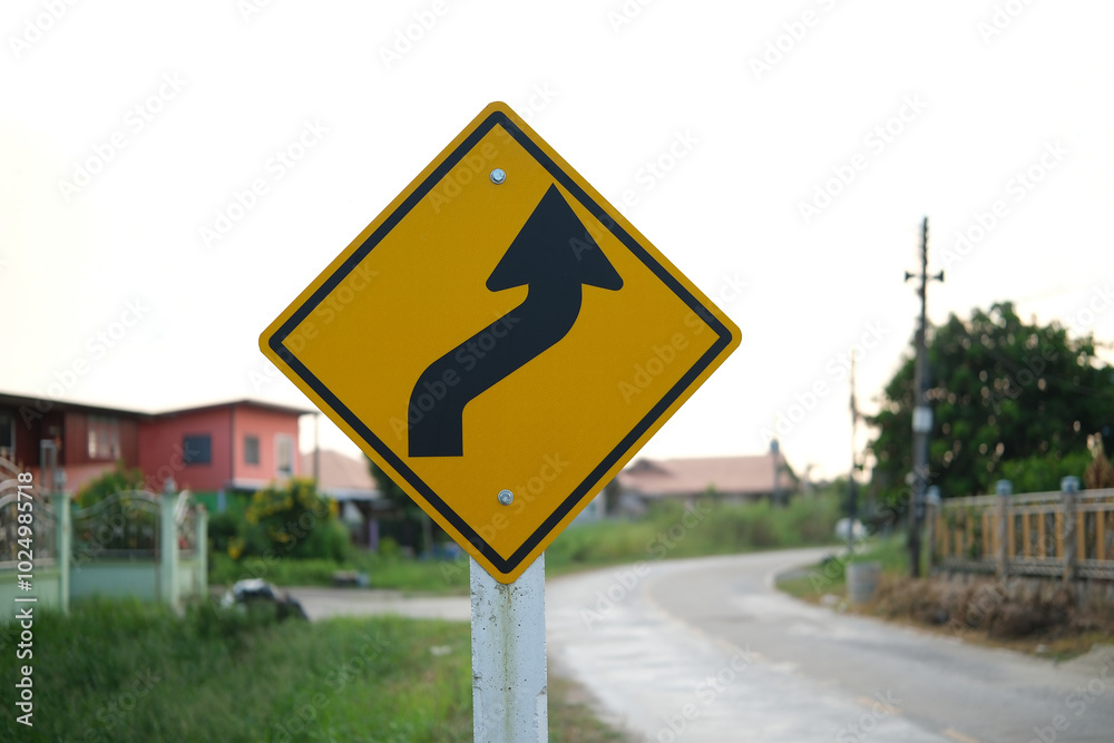 Yellow traffic sign with twisty arrow symbol at rural road Thailand to warn drivers be careful ...
