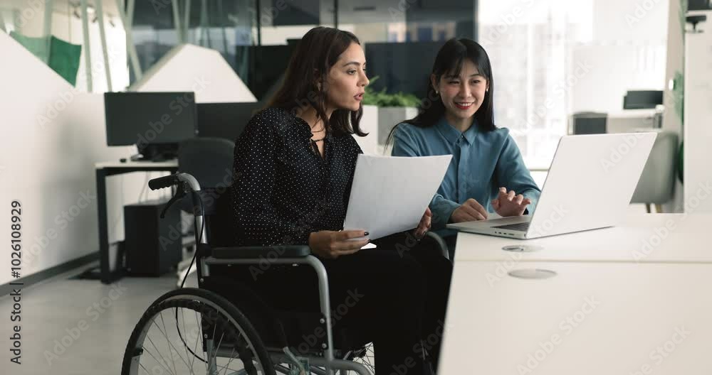 Female employee in wheelchair talking to colleague working on joint ...