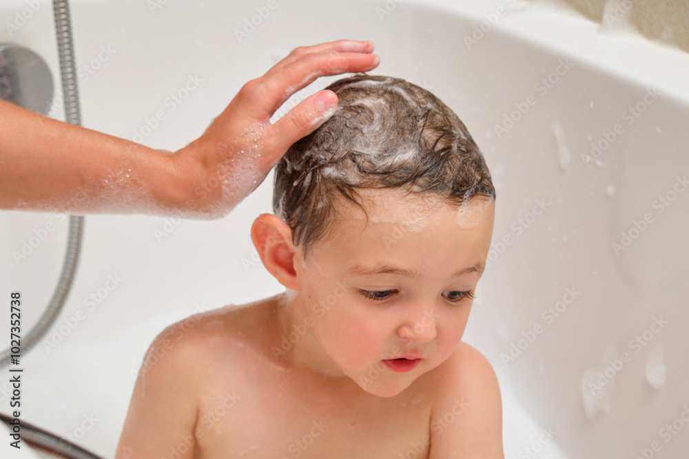 A baby is being washed in a bathtub by a woman. The mother is gently ...