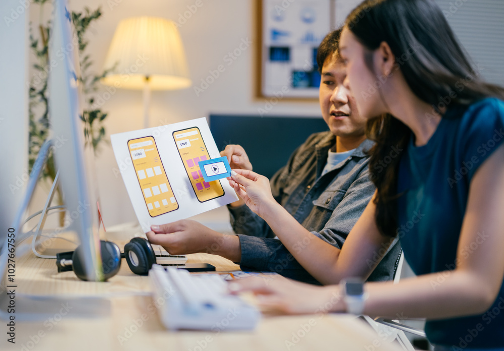 Two Asian Ui Ux Designers Are Discussing A Mobile App Wireframe Prototype At Their Desks In The