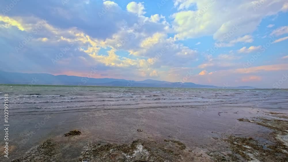 At the edge of a receding lake, majestic mountains and clouds frame the ...