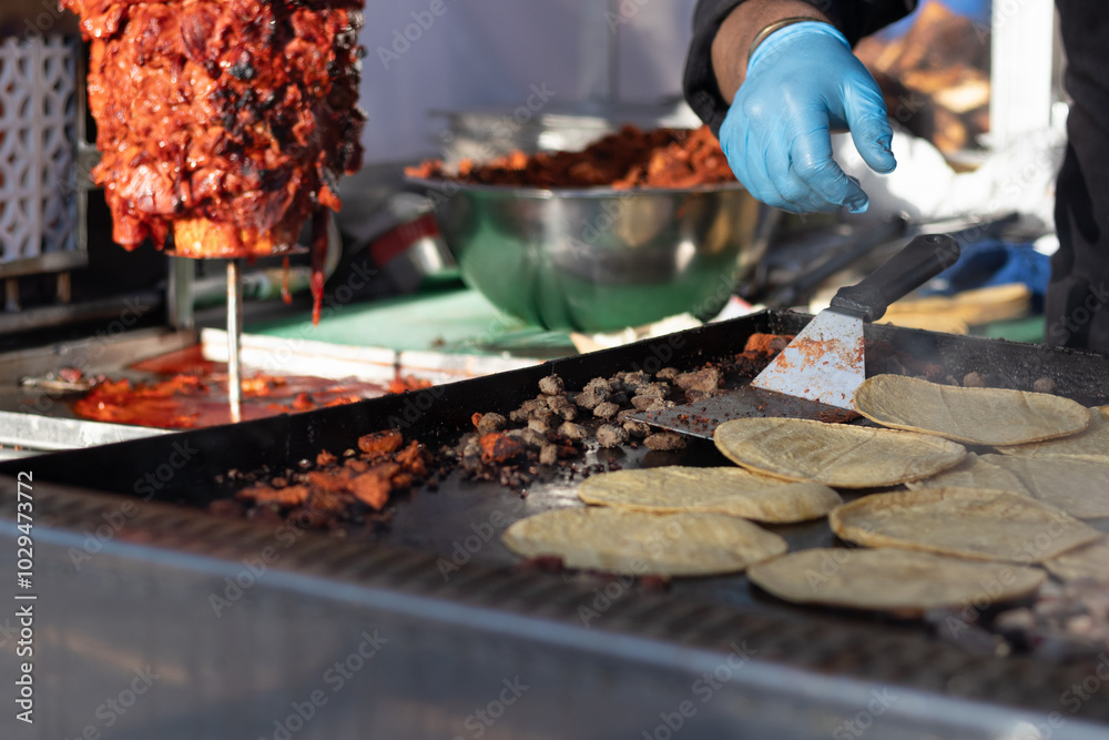 Street vendor grilling tortillas and chopped al pastor meat on a grill ...