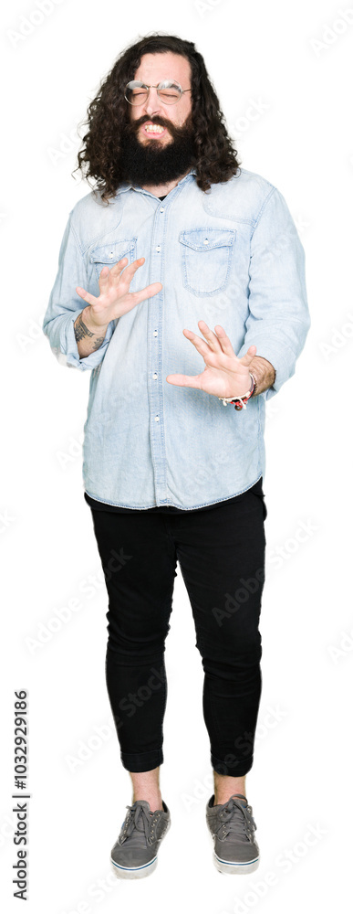 Young hipster man with long hair and beard wearing glasses disgusted ...