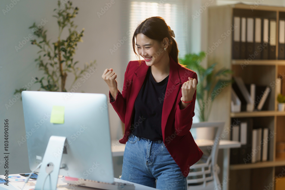 Young businesswoman is raising her arms in front of her computer in her ...