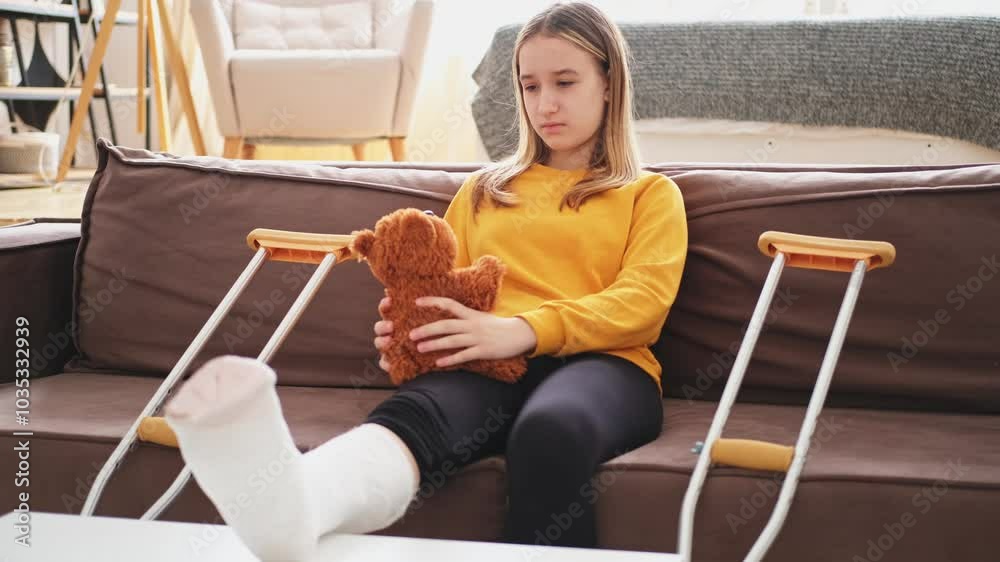 Young girl with broken leg cast sitting on sofa. Sad little kid hugging ...