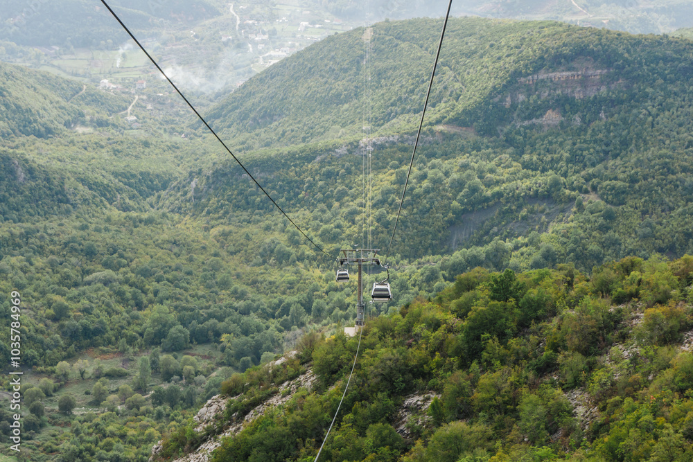 Cable car suspended over a dense forest with mountain and valley views ...