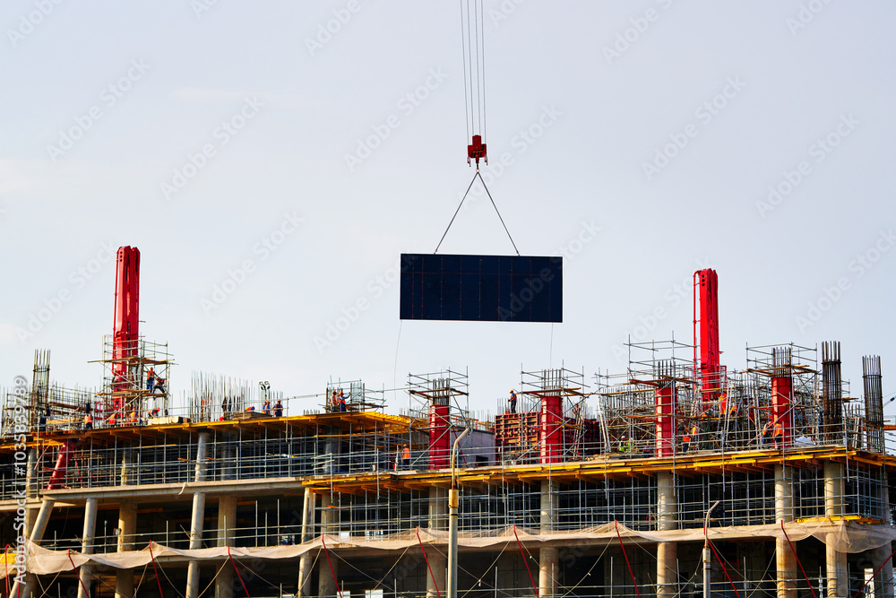 Industrial crane lifting concrete slab at busy construction site with ...