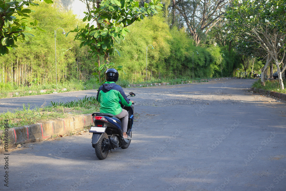 Back view of online taxi rider wearing green jacket and helmet, riding ...