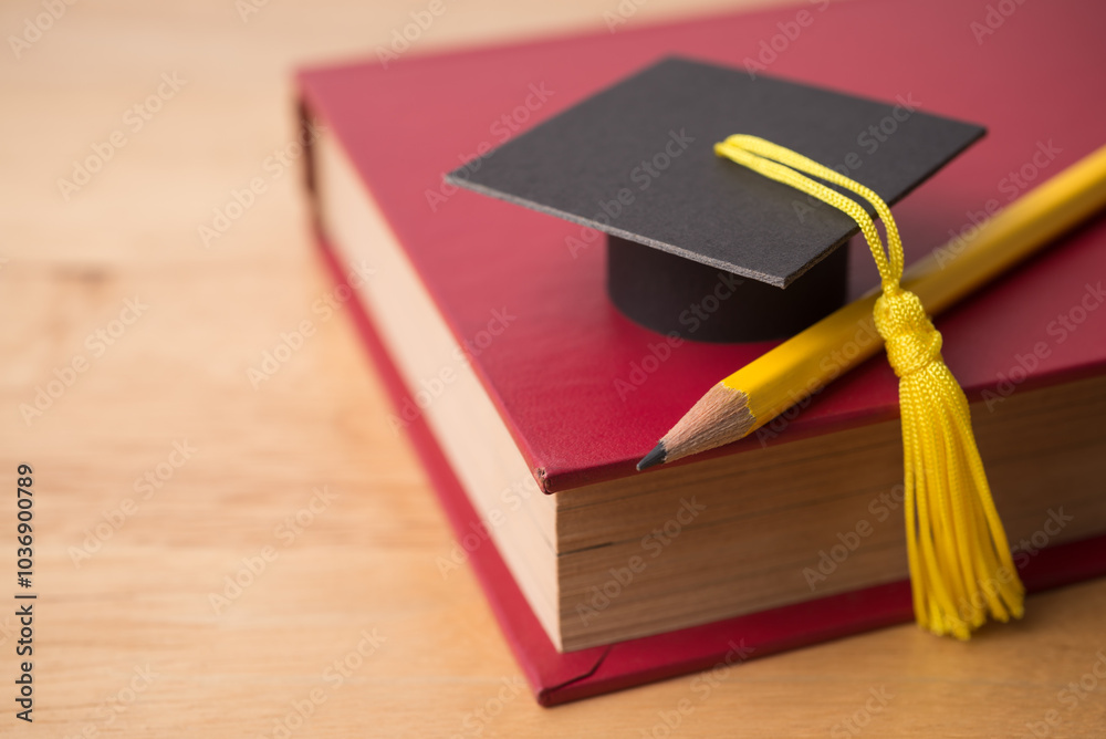 Small graduation cap and yellow pencil on red textbook with wooden ...