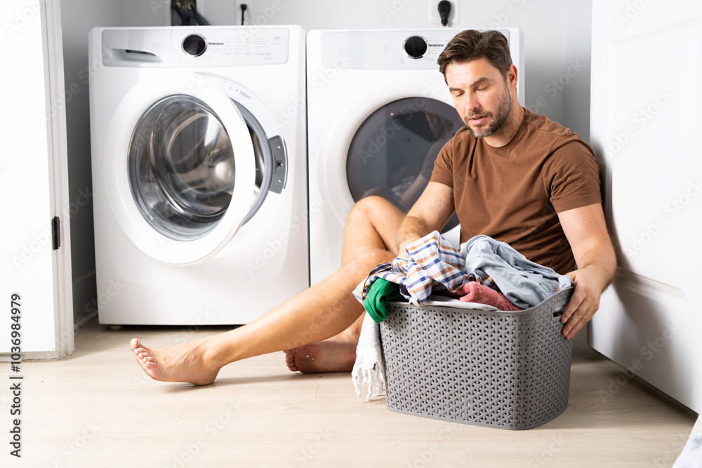 Happy man sorting clothes near washing machine in laundry room. man ...