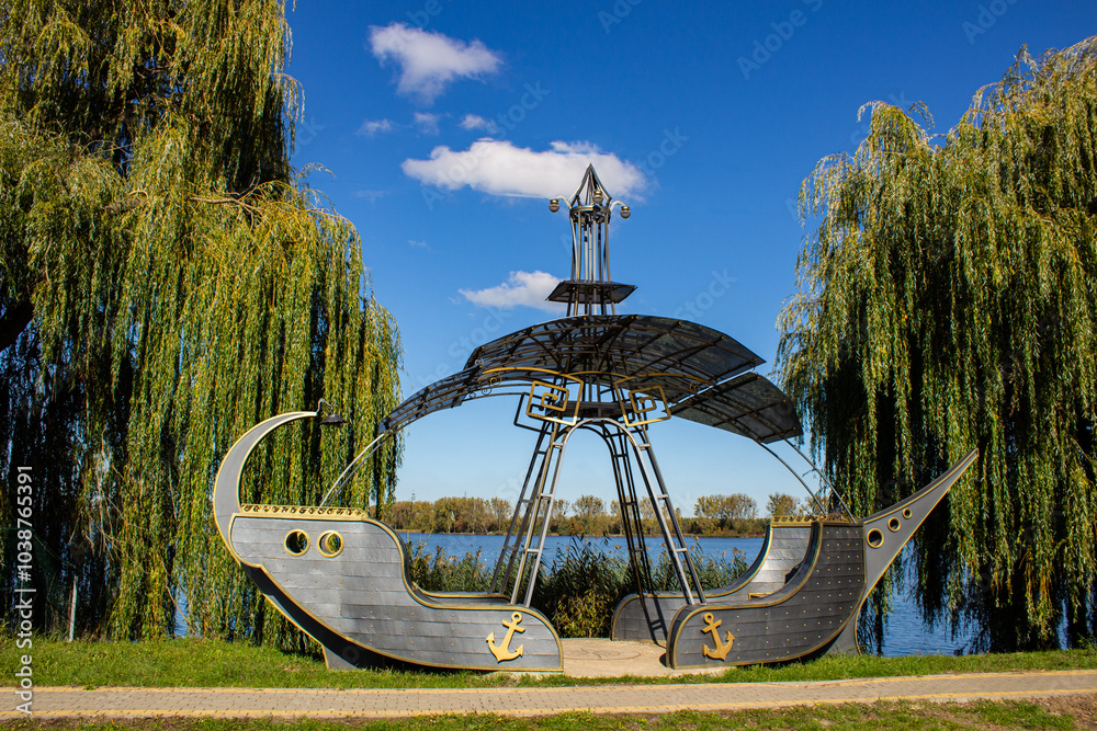 The photo shows a metal sculpture in the shape of a ship on the shore ...