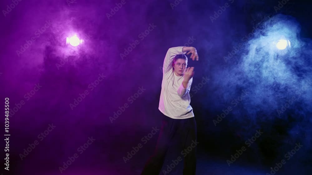 Mysterious female figure dancing in dark studio with smoke and purple ...