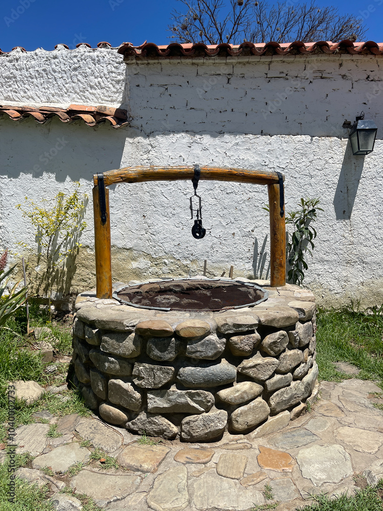 Rustic stone water well in a garden with white wall and blue sky. Stock ...