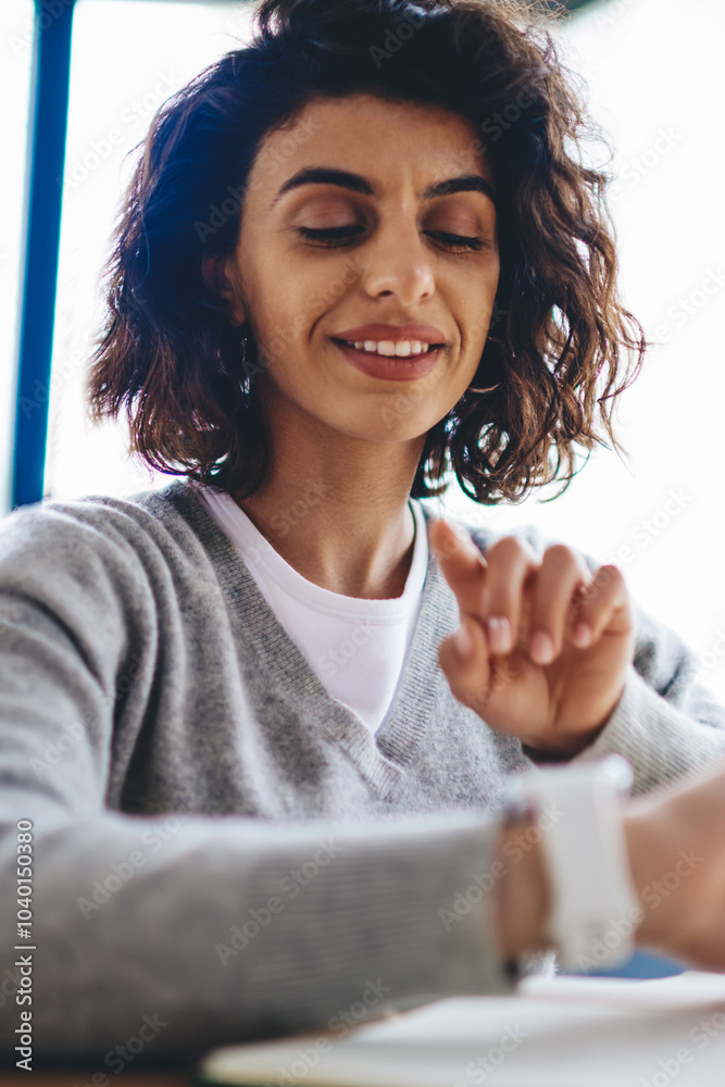 Smiling young woman in casual wear looking at smartwatch and checking ...
