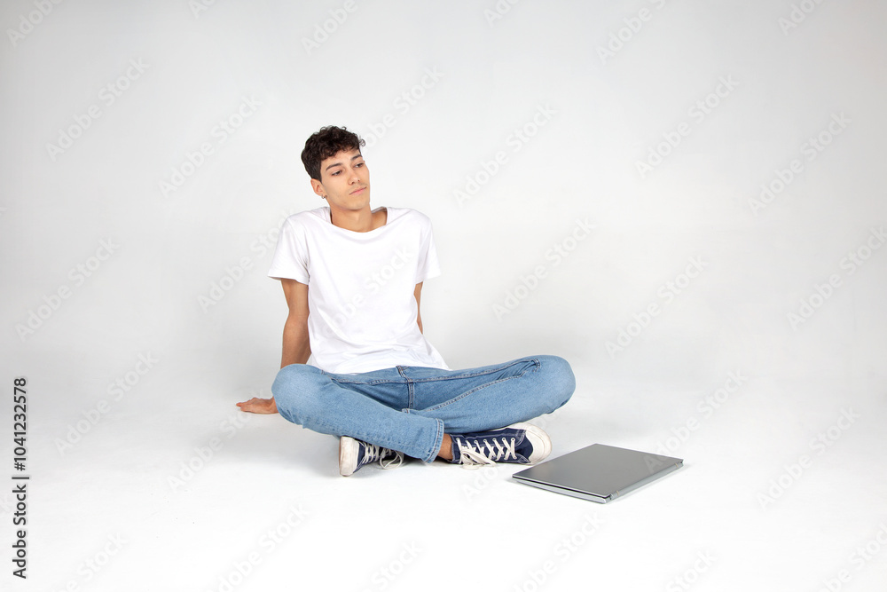 Chico sentado en el suelo con vaqueros y camiseta blanca, mirando un ...