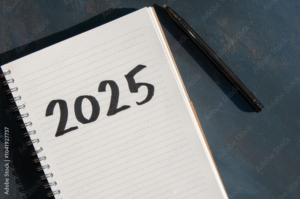 Notebook with "2025" written on the page, next to a pen on a dark ...