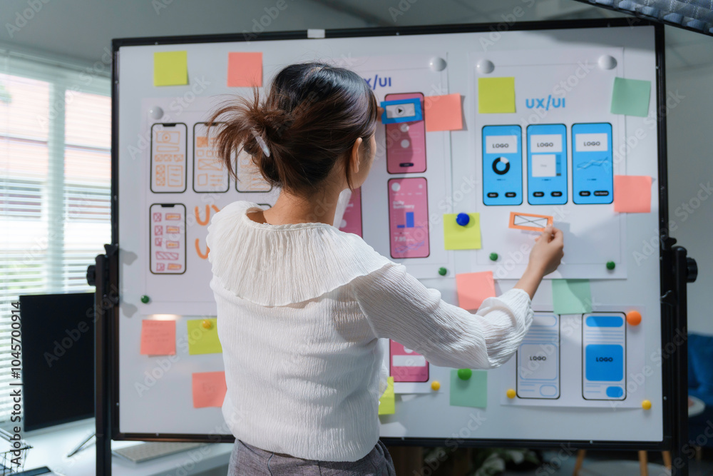 Young professional is sticking a note on a whiteboard while working on ...