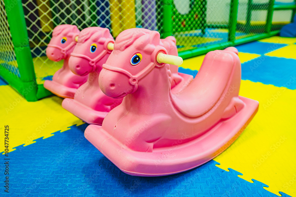 Colorful pink rocking horses in an indoor play area for children with ...