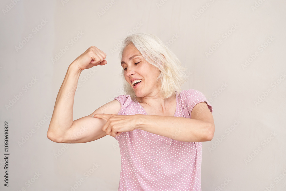 Confident senior woman flexing arm muscles in polka dot shirt shows ...