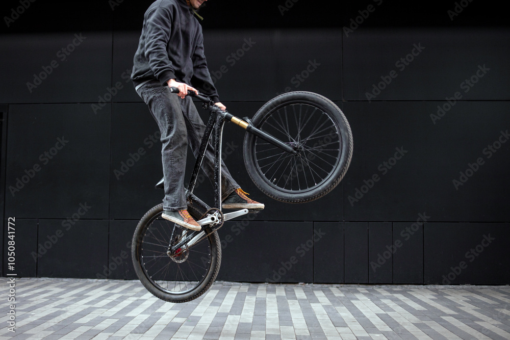 young hipster guy doing stunts on a bike in the city against the ...