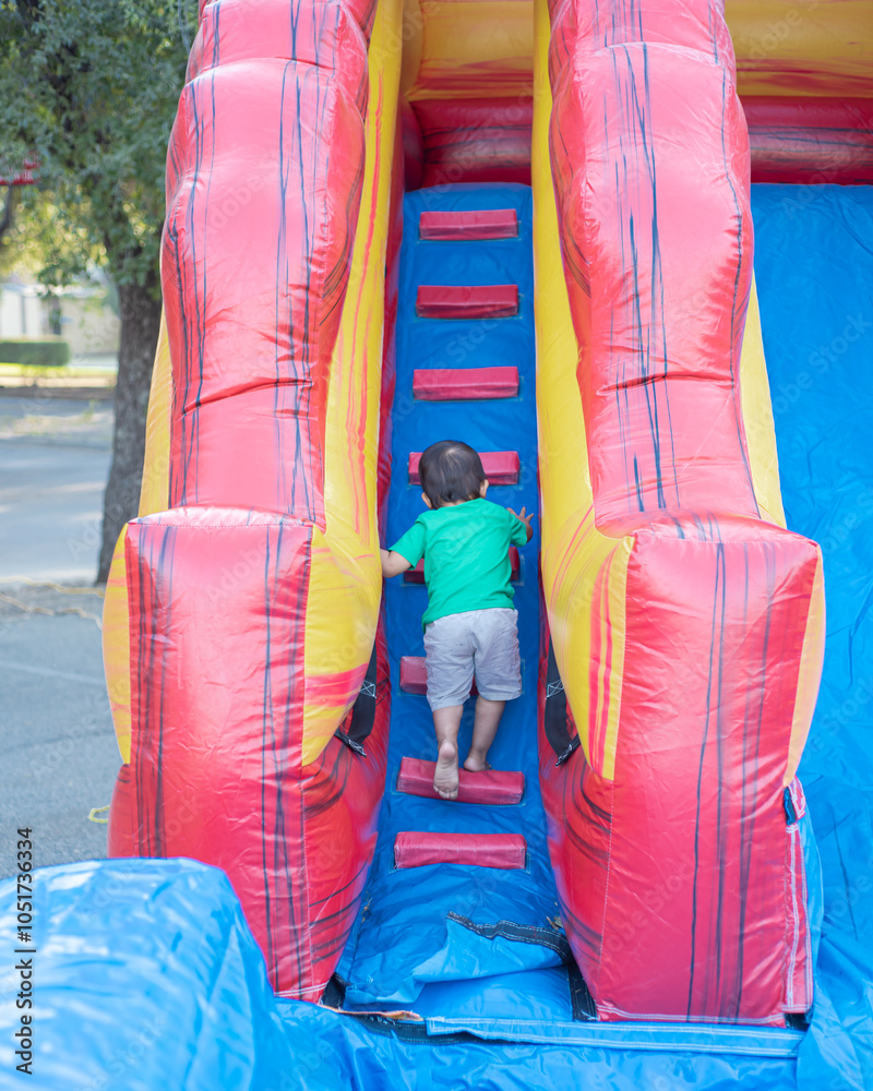 Baby boy climbing ladder of inflatable bounce house jumping castle ...