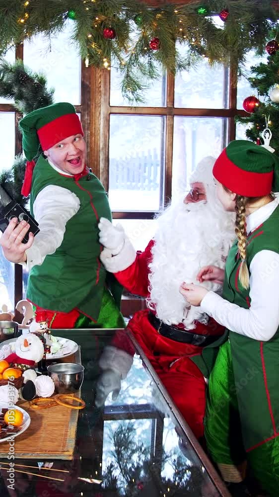 Funny elves and Santa in costumes in Santa's residence. Two elves and ...