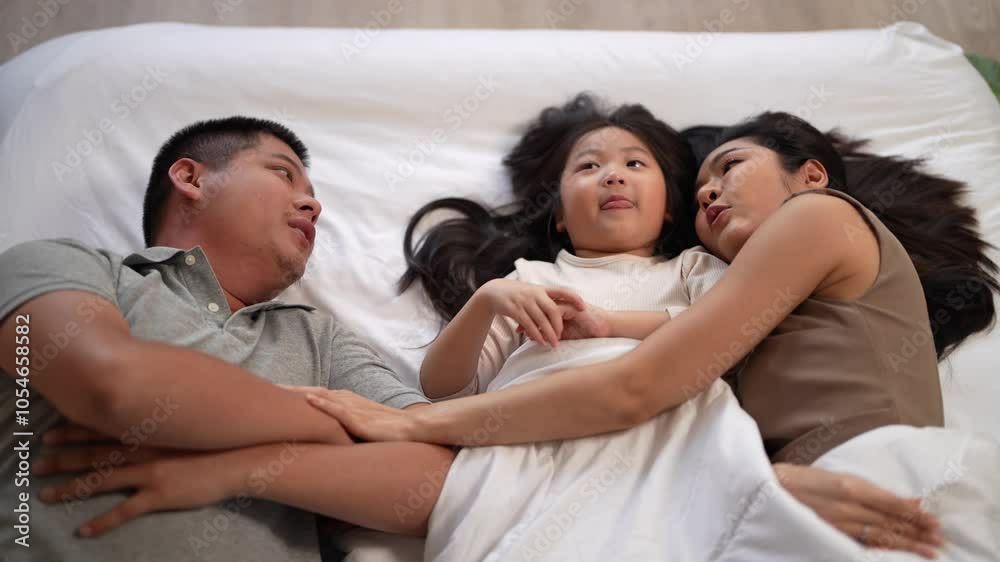 A family of three lies together on a bed, with parents holding hands ...