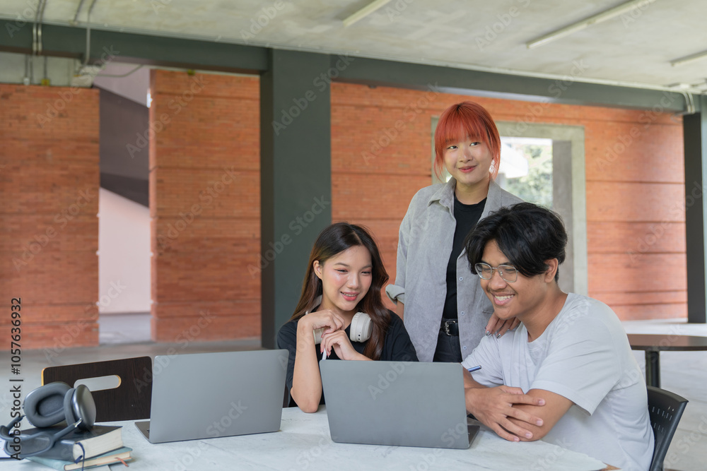 Three young asian students are working together on their laptops ...
