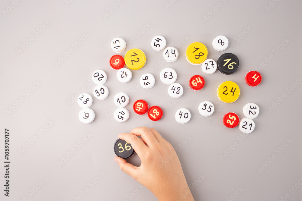 Children hands arranging plastic bottle caps with hand-written numbers ...