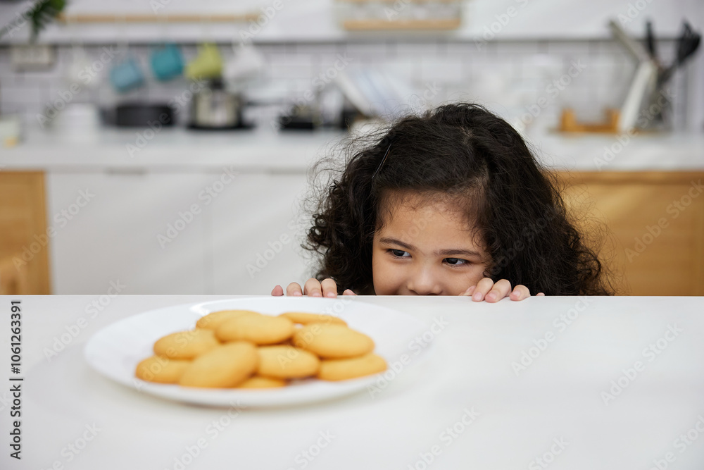 child girl hiding and looking butter cookies or biscuits on dish from ...