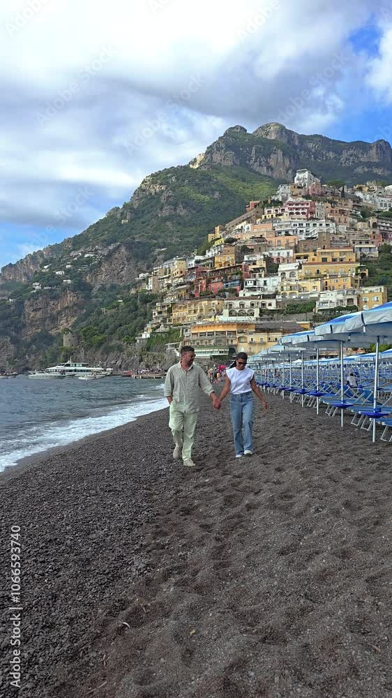 Two friends enjoy a leisurely walk on a pebbled beach in Positano ...
