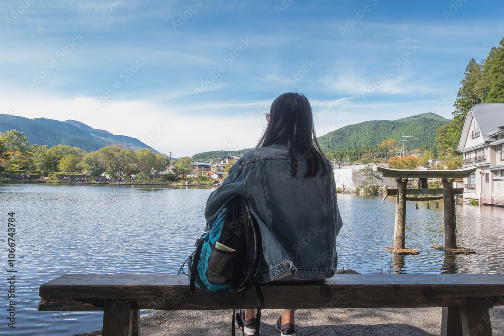 Woman sitting on the chair at Lake Kinrin and Japanese gate (Torii) with Mount Yufu and blue sky ...