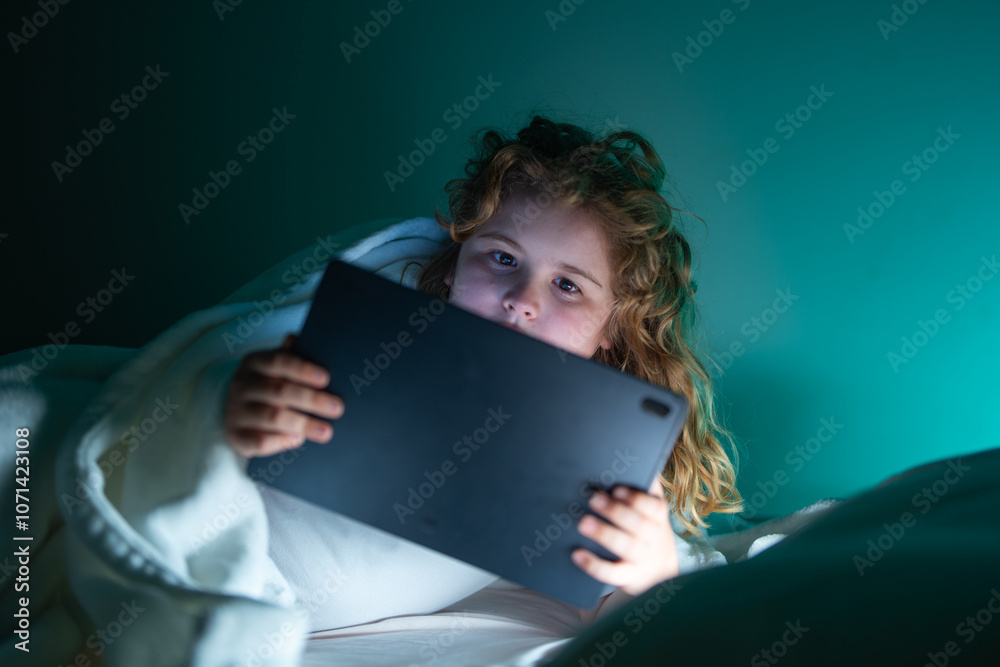 Kid lying on bed and surfing Internet on tablet in dark room. Boy ...