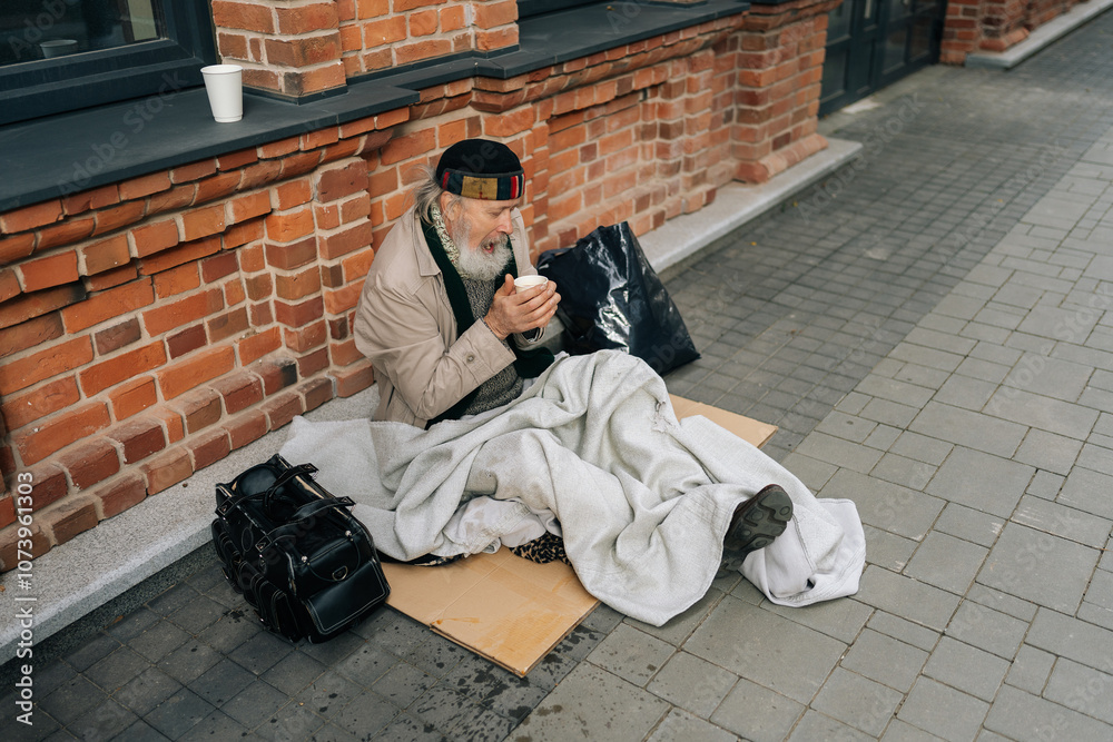 High-angle view of freezing aged homeless man sitting on city street ...