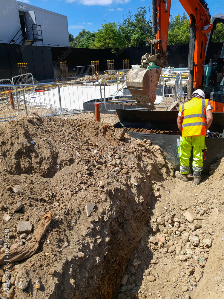 Construction worker and excavator performing trench excavation and site ...