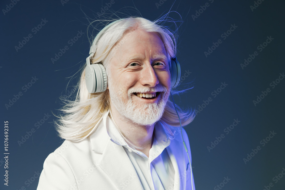 Happy senior man with long white hair wearing headphones against a blue ...