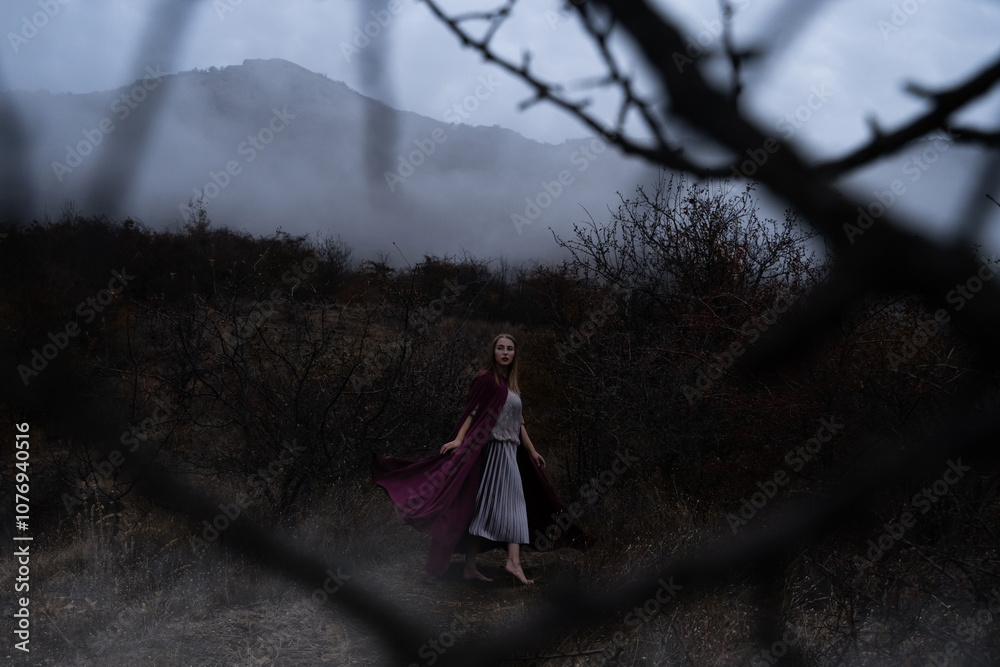 Young witch stands and looks back in fantasy dark forest, long red ...